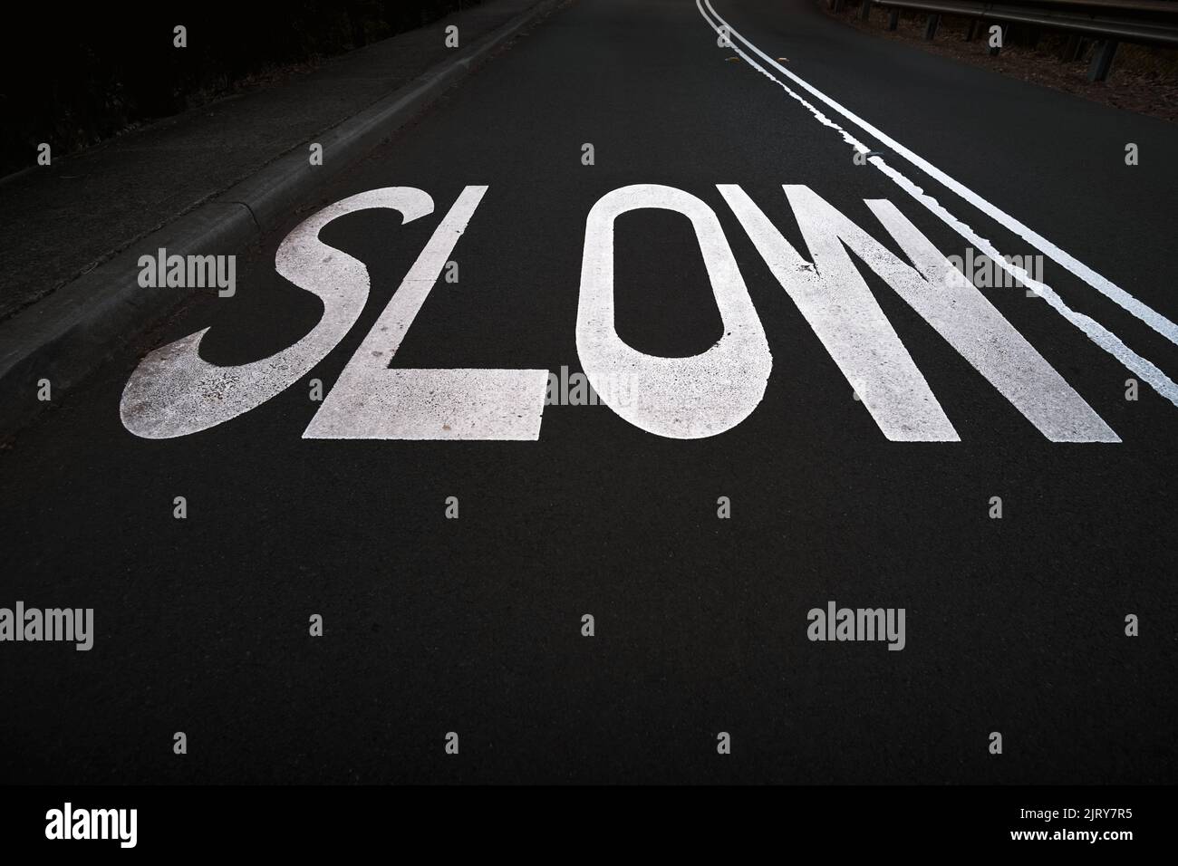 SLOW road sign painted on bitumen asphalt road in white paint. Low wide ...