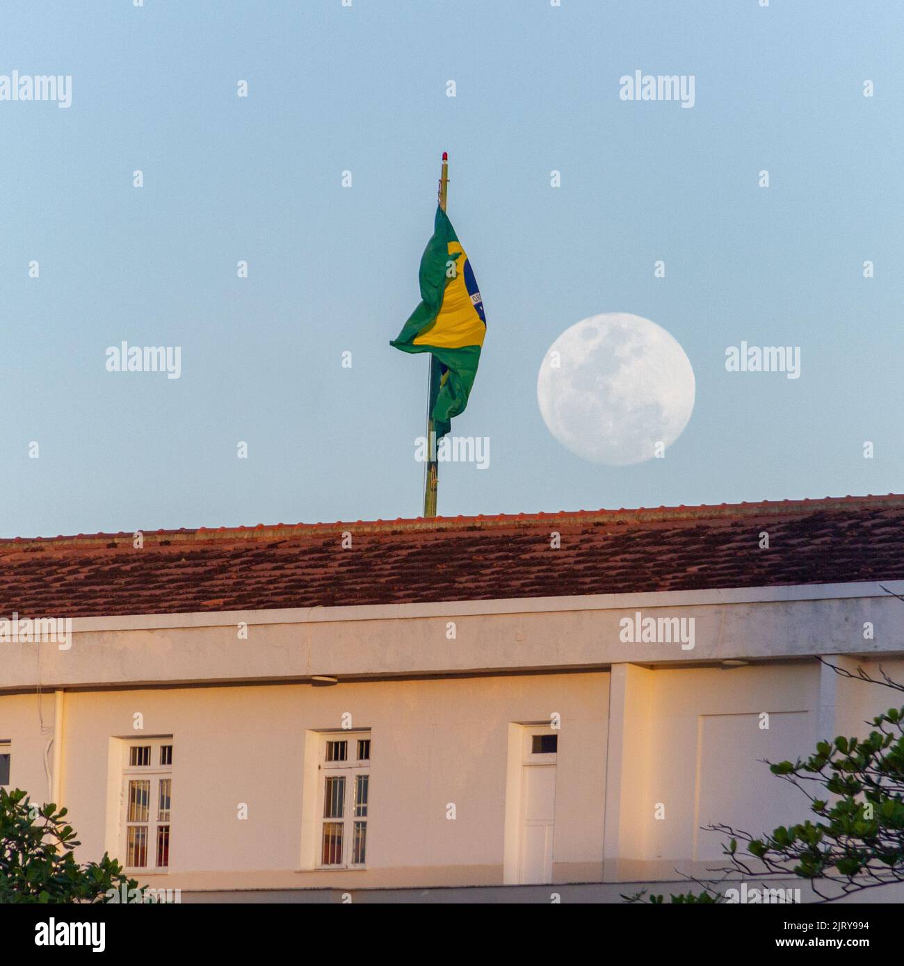 full moon rising beside the flag of brazil on the roof of the ...