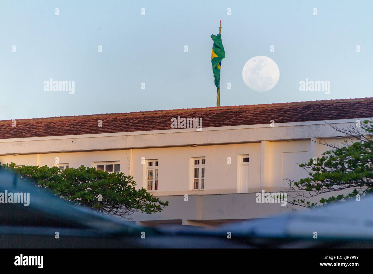 full moon rising beside the flag of brazil on the roof of the ...