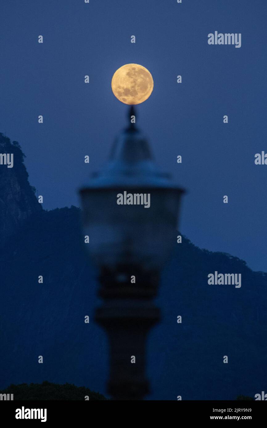 full moon setting behind a light pole early in the morning in the city ...