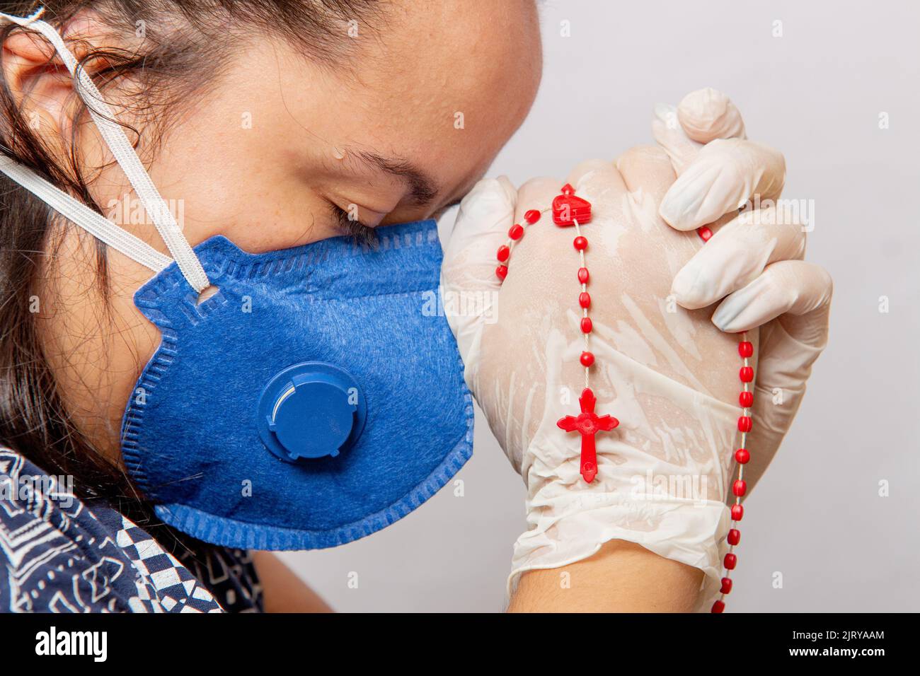 white woman praying wearing blue mask with a third in her hands ...