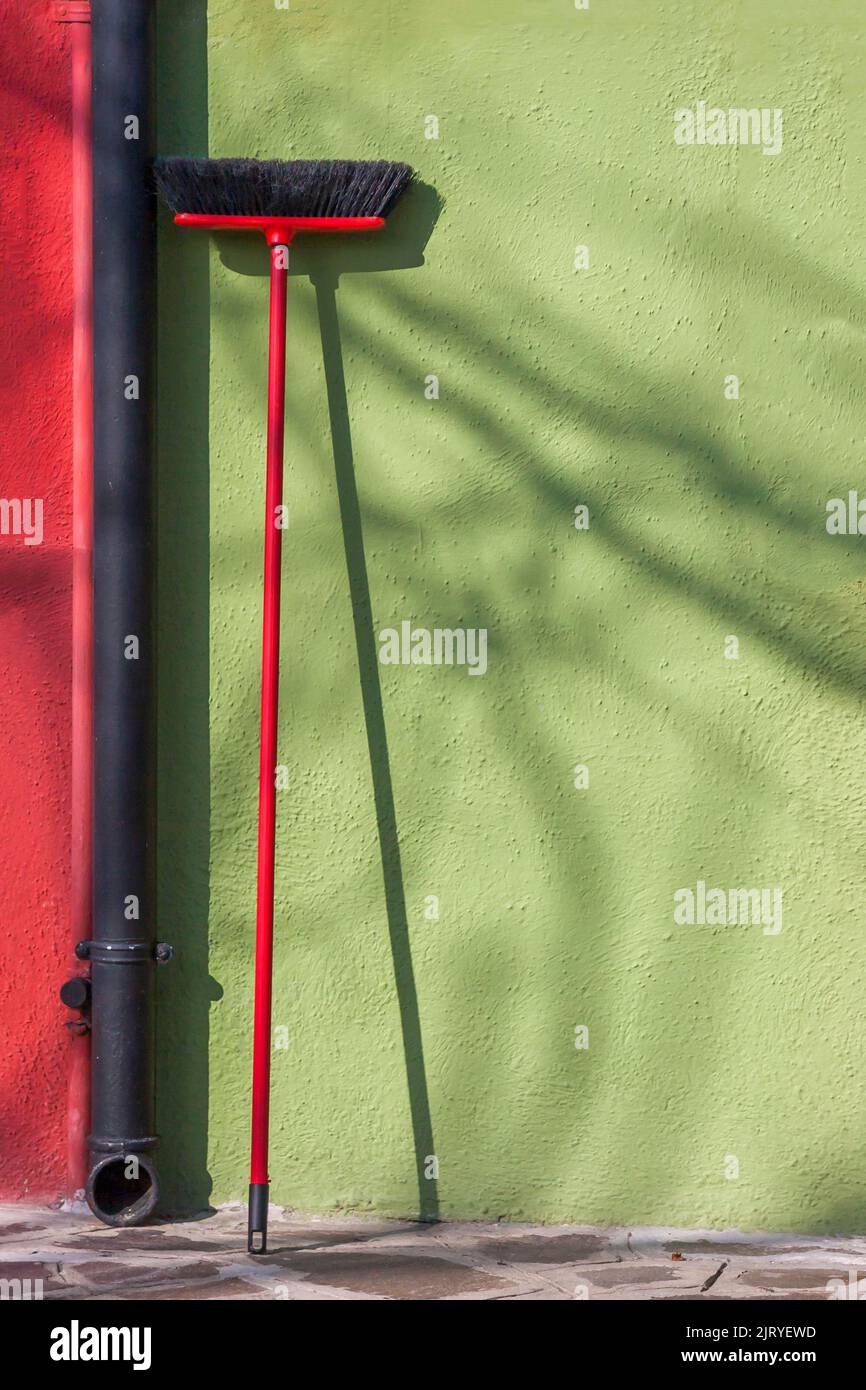 Red broom leaning against a green house wall, Italy Stock Photo - Alamy