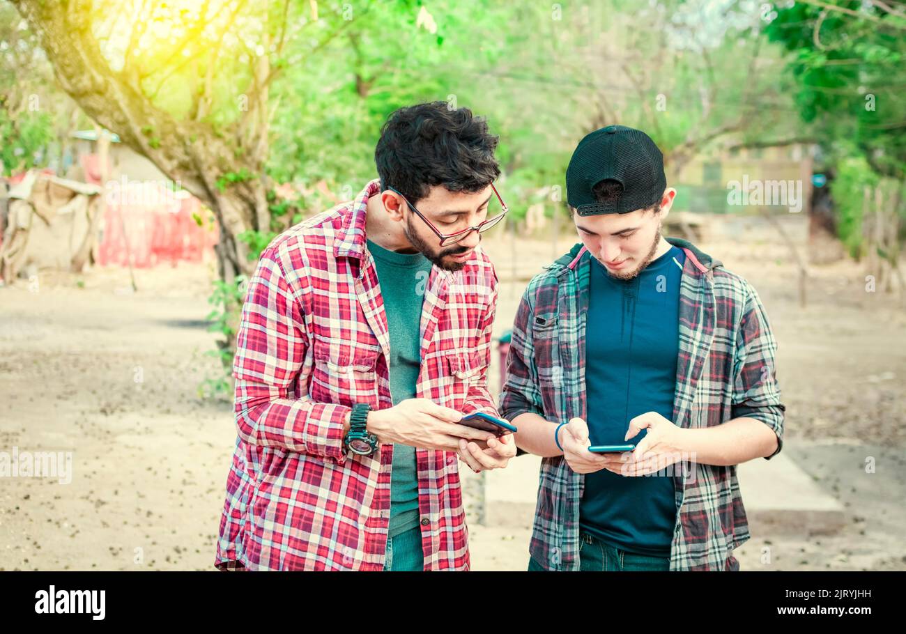 Two teenage guys pointing and checking their cell phones, Two friends ...