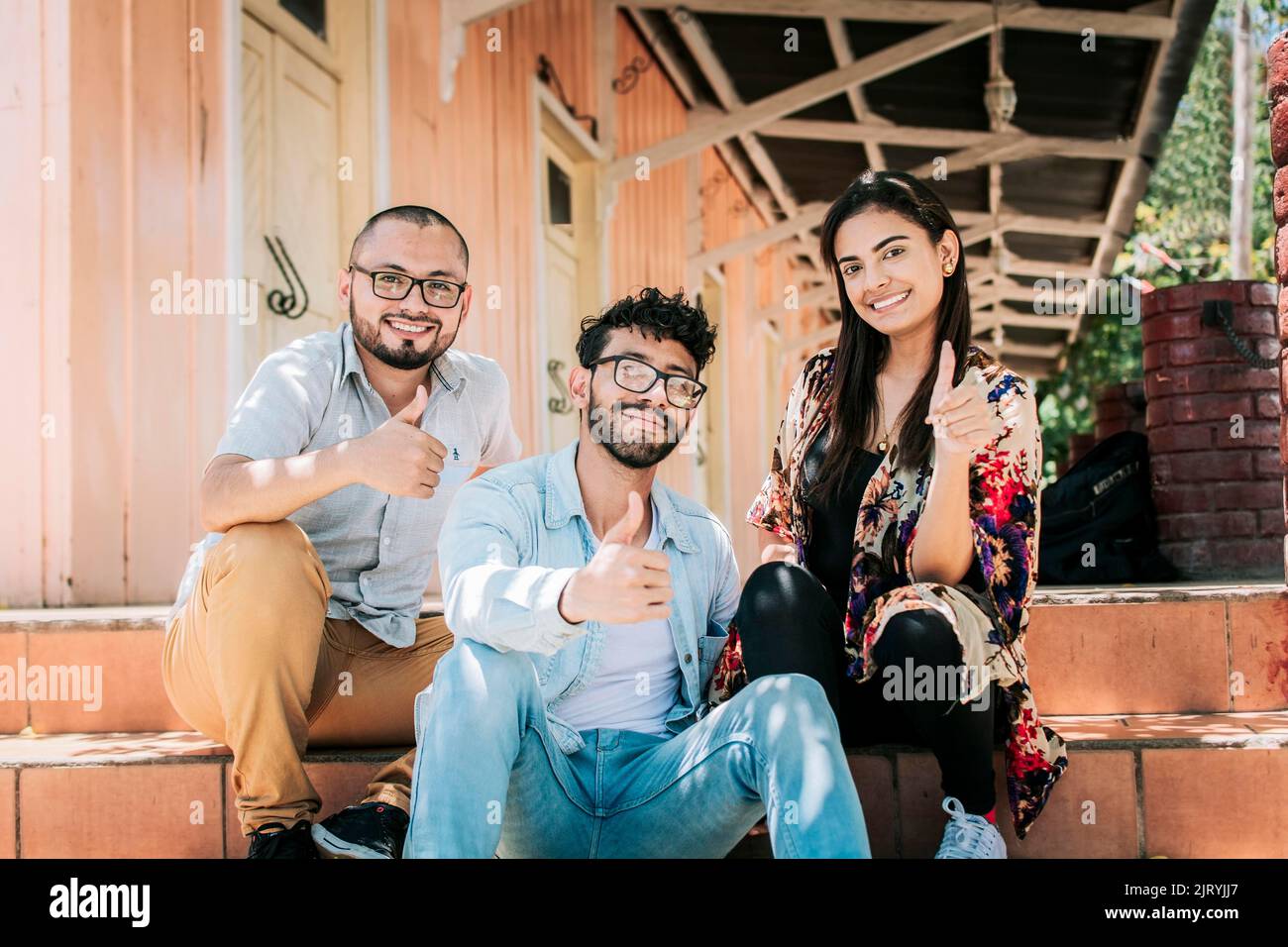 Group of happy friends sitting on the stairs giving thumbs up. Portrait ...