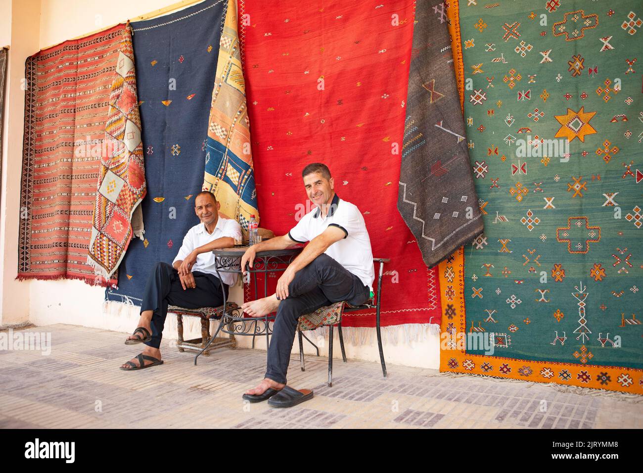 Moroccan men taking a coffee break, hand-knotted carpets hanging on the ...