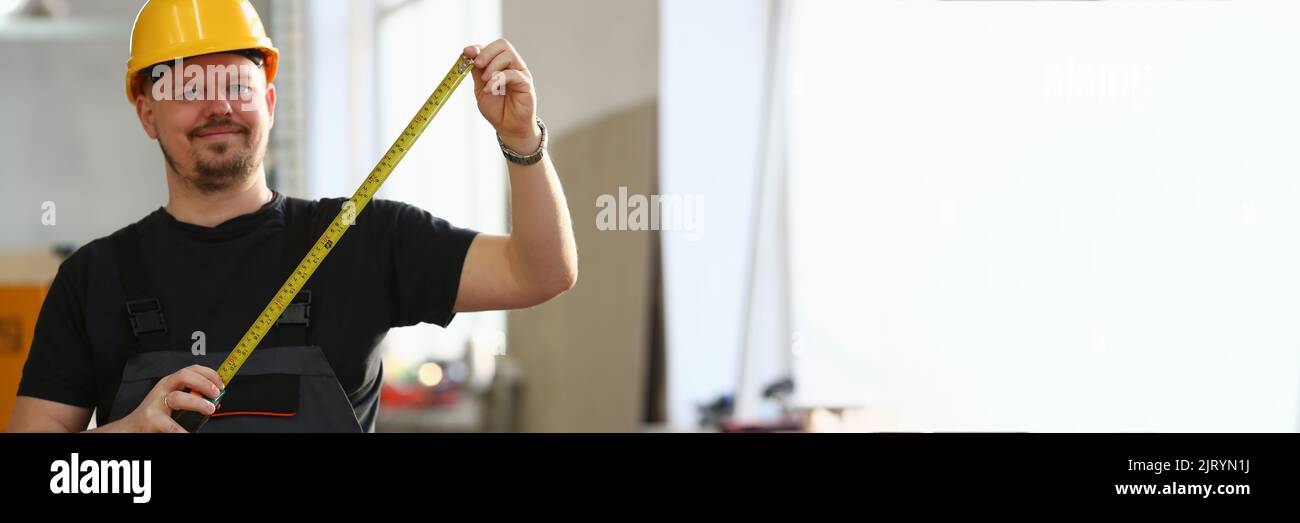 Worker in helmet and uniform holds tape measure Stock Photo - Alamy