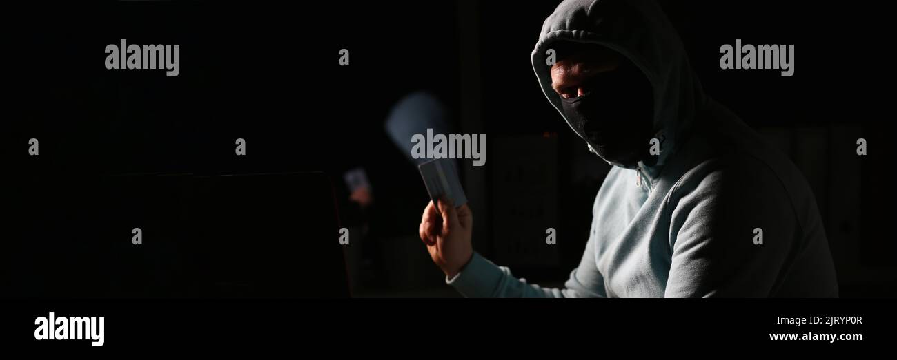 Hacker in dark jacket looking at laptop screen in dark room is holding ...