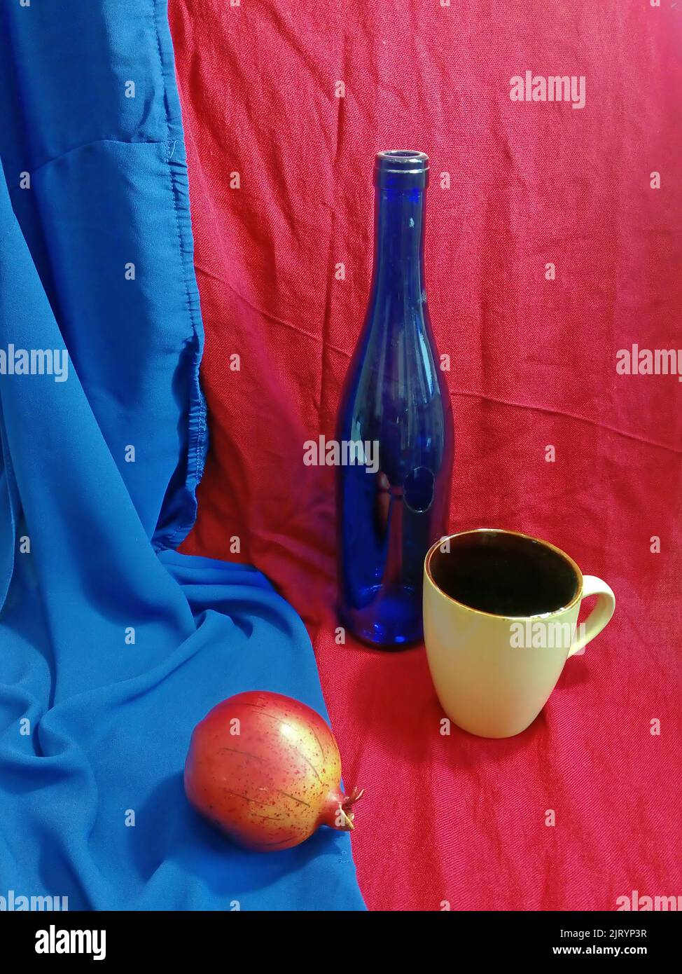 Still life of blue bottle on red drapery and pomegranate on blue one ...
