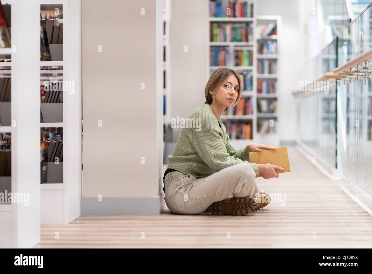 Middle-aged woman reader sitting on floor with book in hands in modern ...