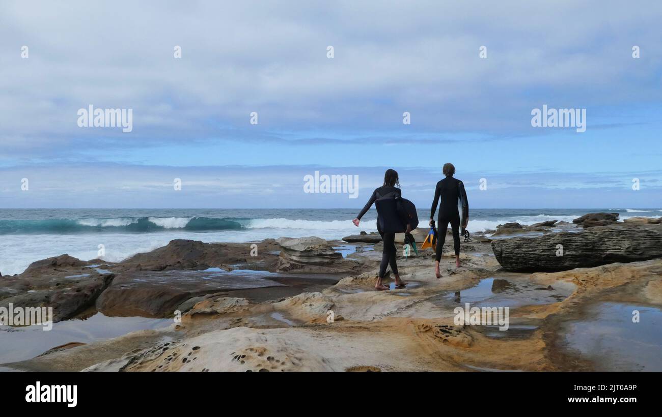 rear view of two young people carrying boogie boards and flippers ...