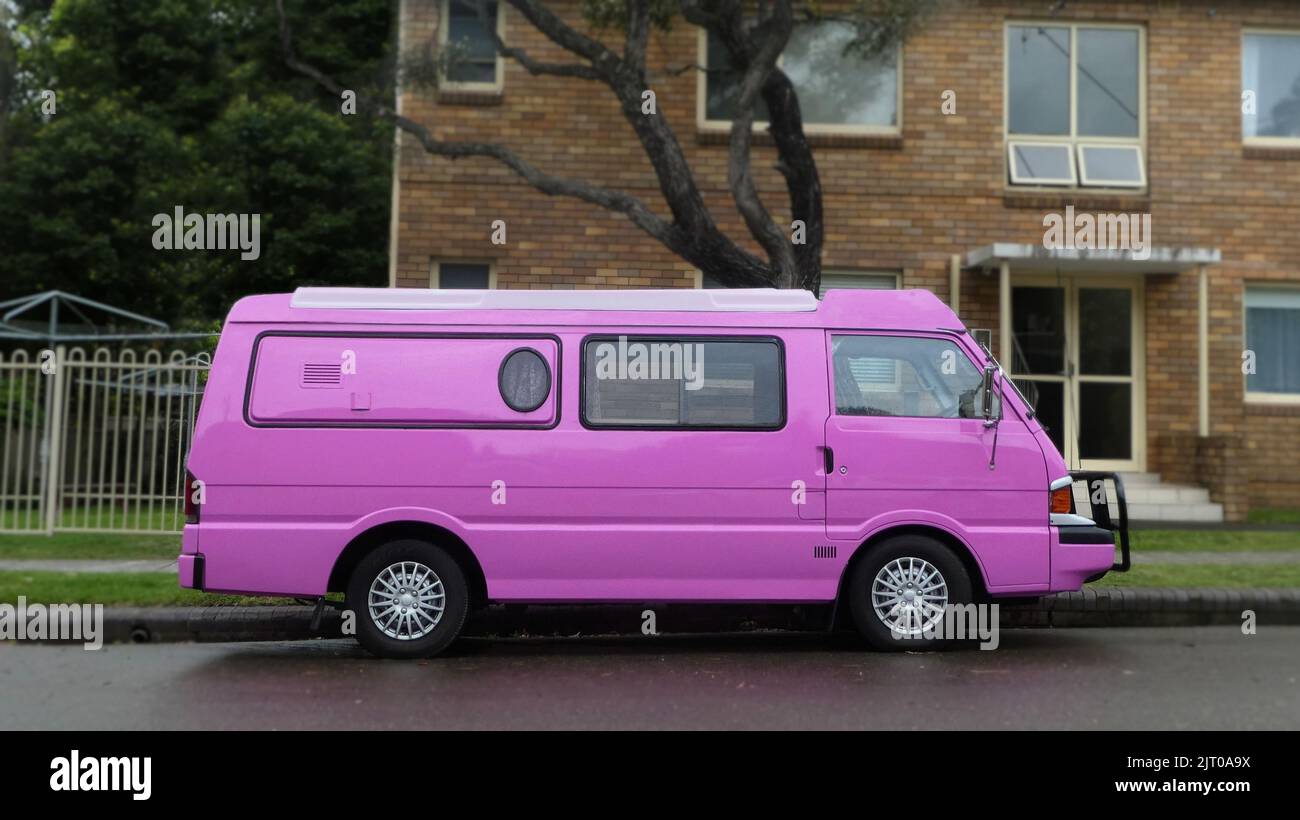 side view of pink camper van parked outdoors on street in front of ...