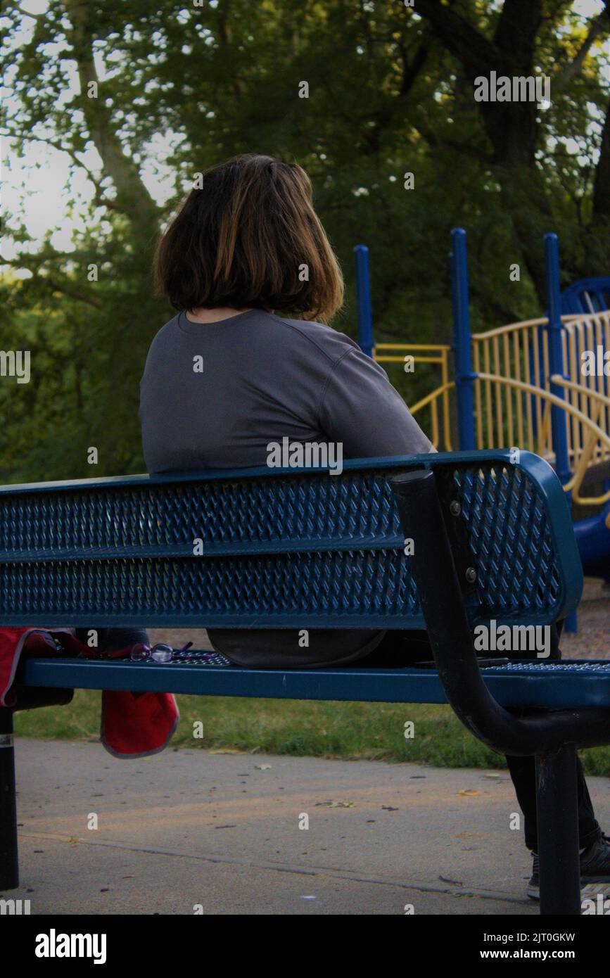 A vertical back view of a female sitting on a bench at the children's ...