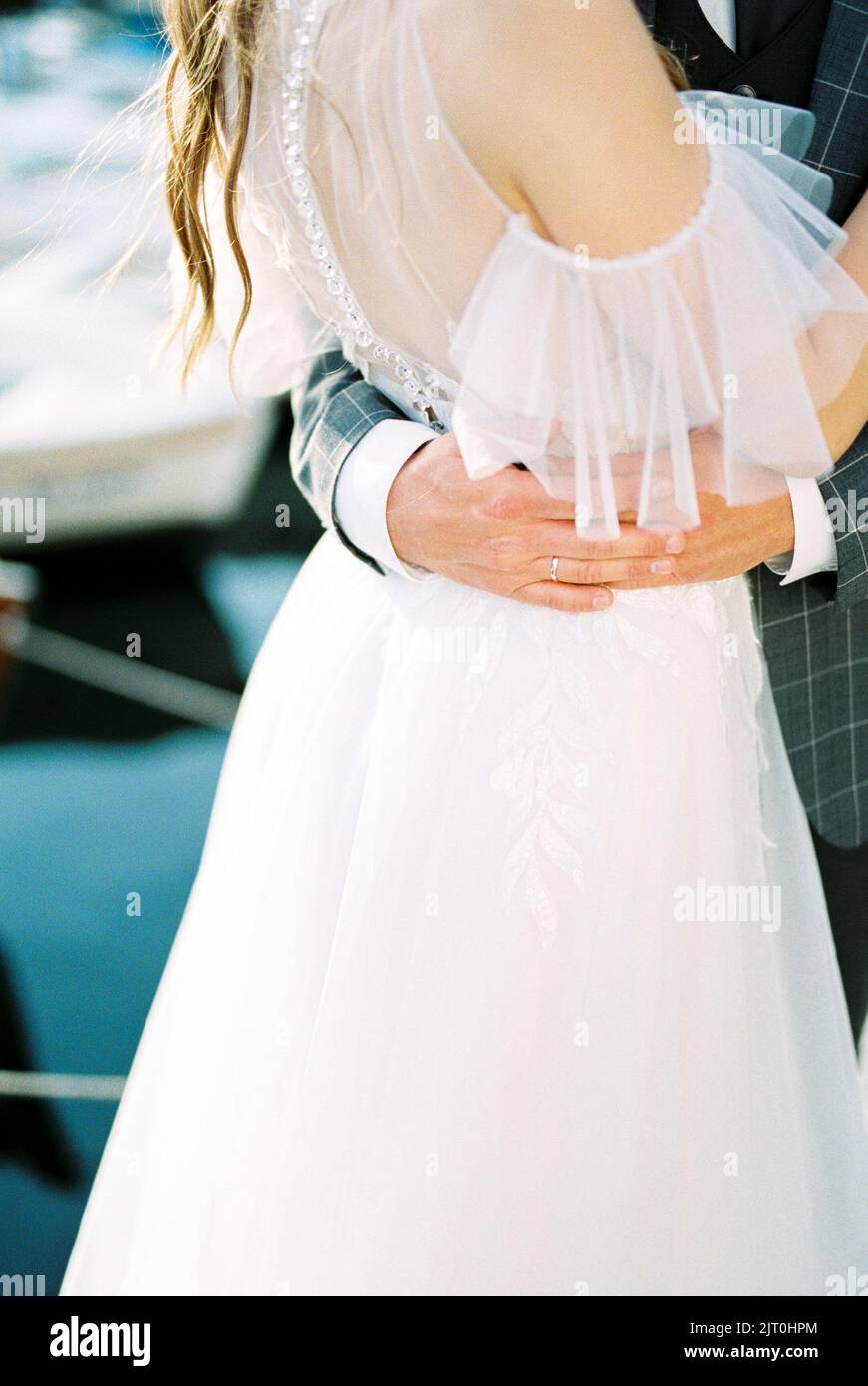 Hands of groom in a plaid jacket hug the waist of bride in a white ...