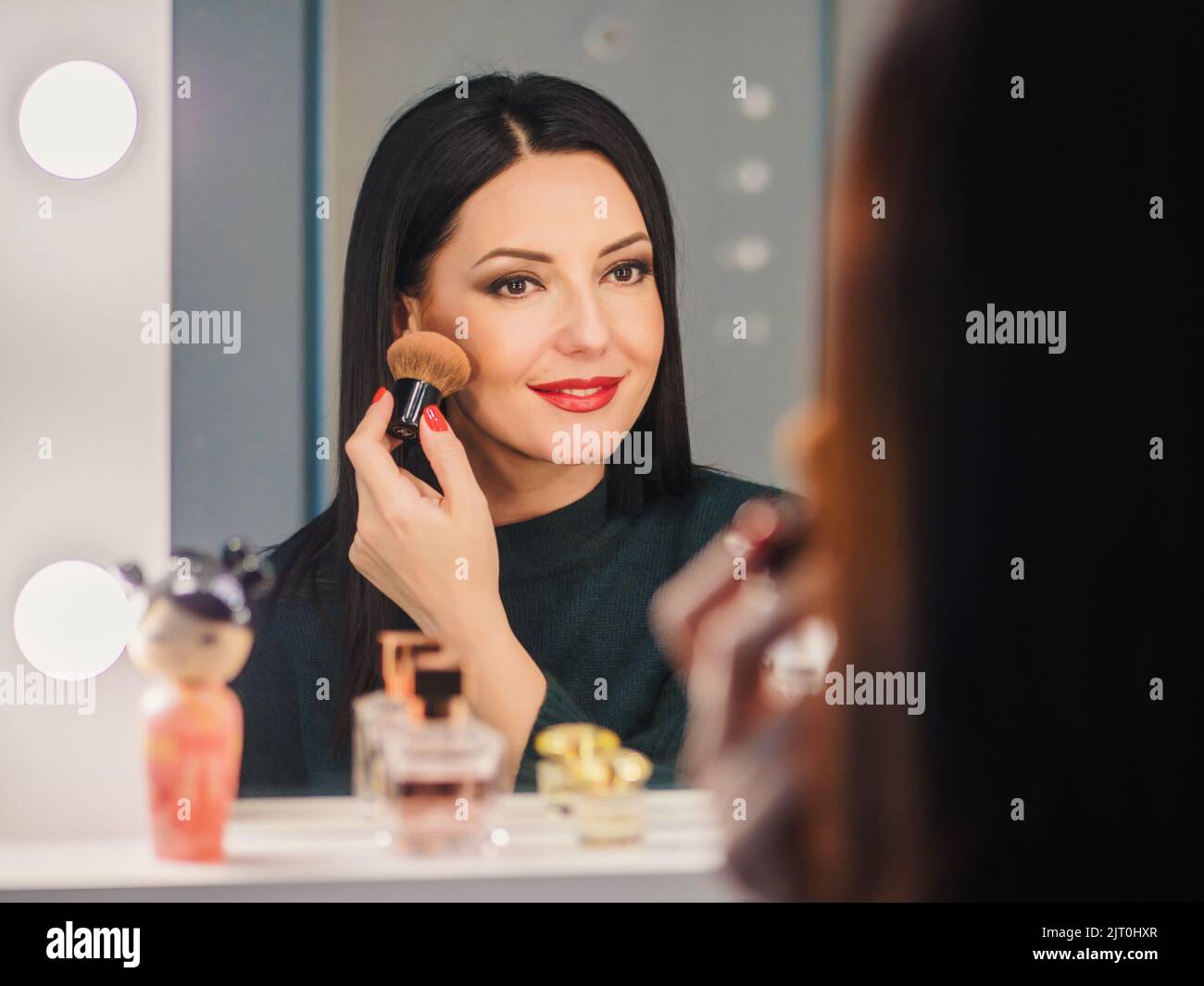 Reflection of lady applying her make-up. Brunette mature woman putting ...