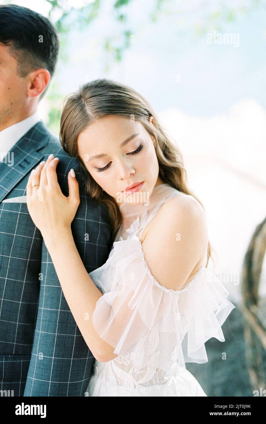 Bride hugs groom from behind with her head on his shoulder Stock Photo ...