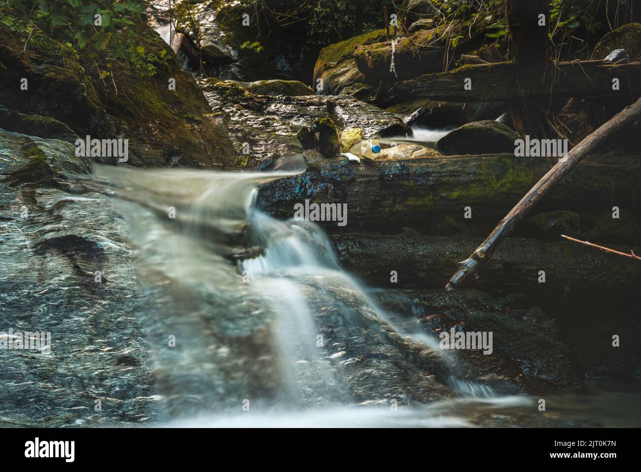 a flowing waterfall with plastic bottle washed up on a rock Stock Photo ...
