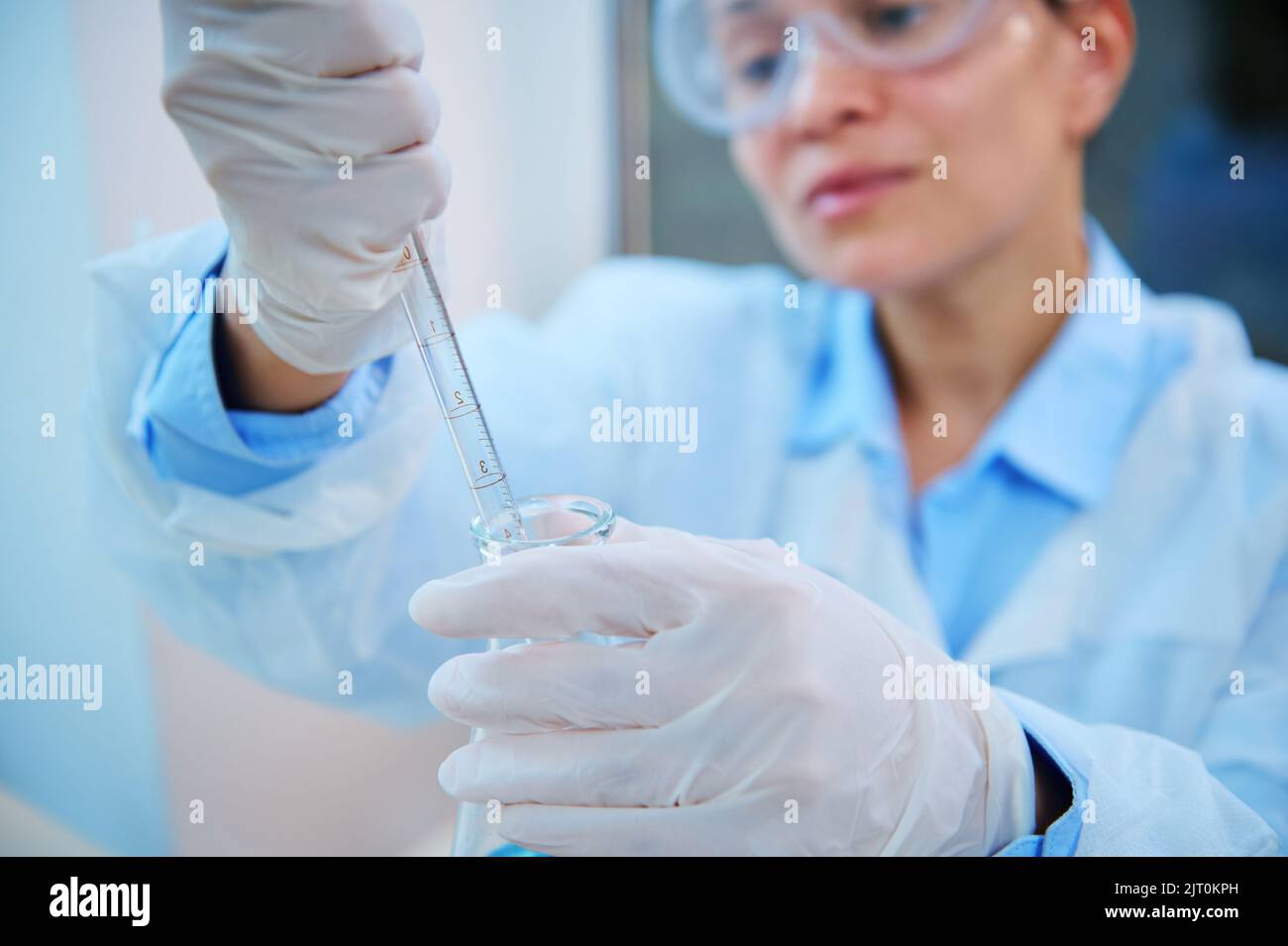 Focus on glass laboratory pipette in gloved hands of a blurred female ...