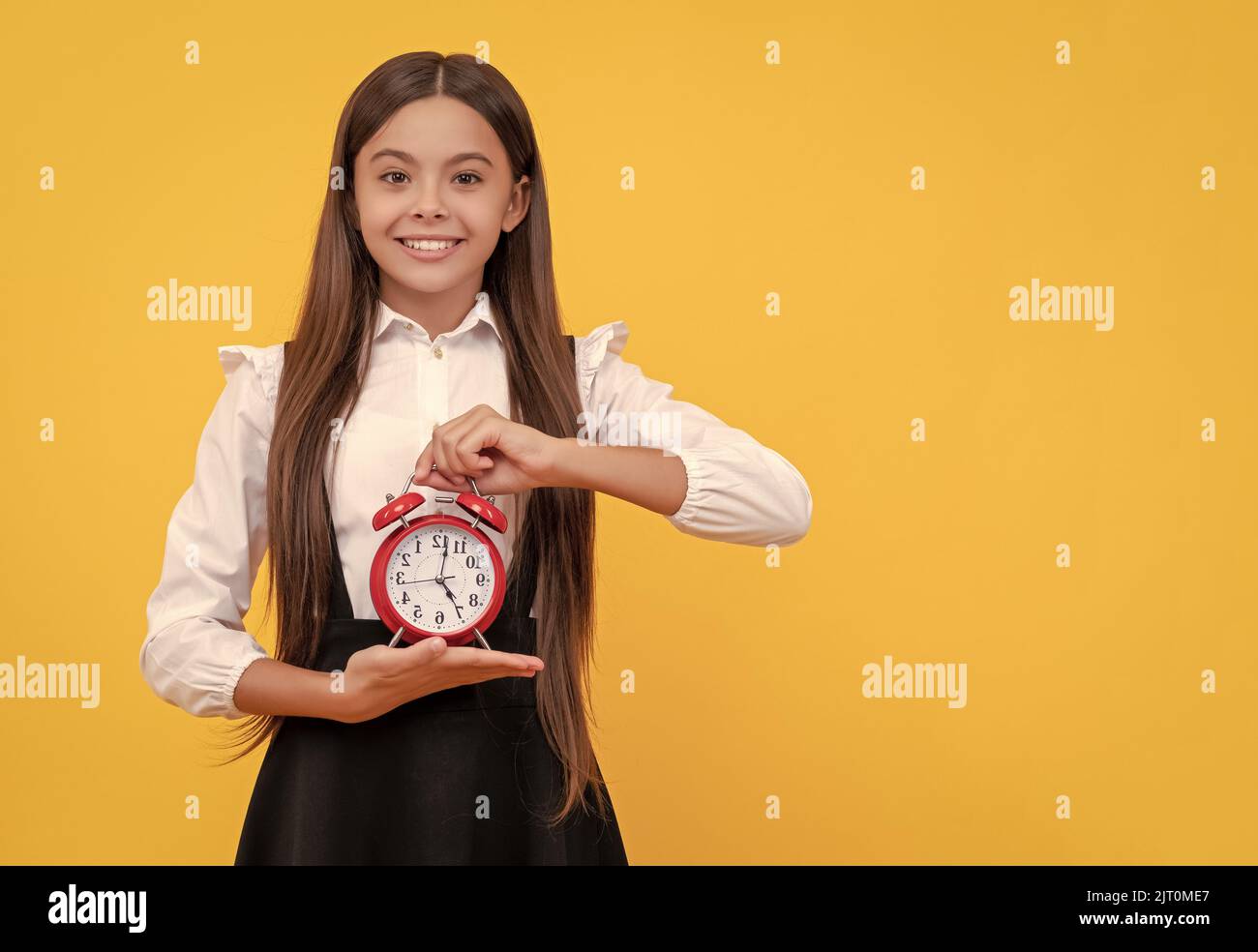 cheerful kid in school uniform with alarm clock showing time on yellow ...