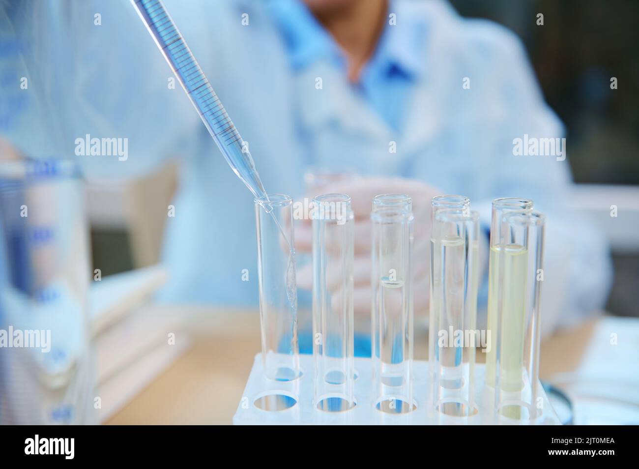Focus on glass pipette with dripping reagent in test tube over blurred ...