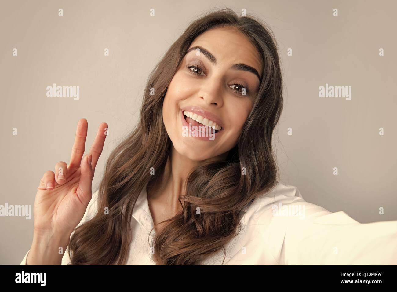 Close-up of young beautiful woman taking selfie. Isolated gray background. Lovely girl posing ...