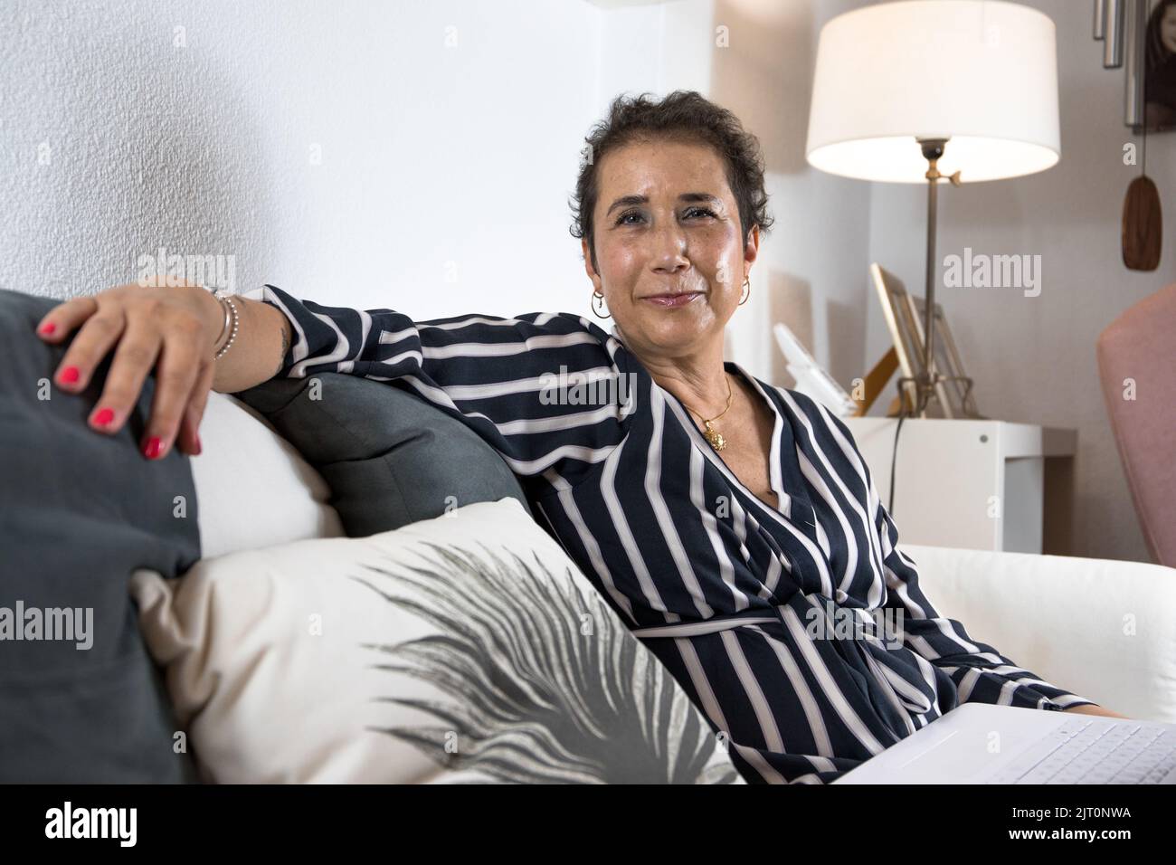 A vertical shot of a 50-year-old cancer overcomer sitting on the sofa ...