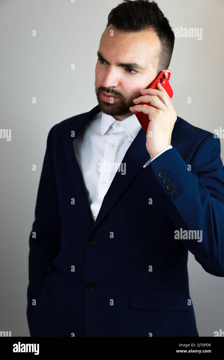 Handsome Caucasian man in a navy blue suit talking by his red phone ...