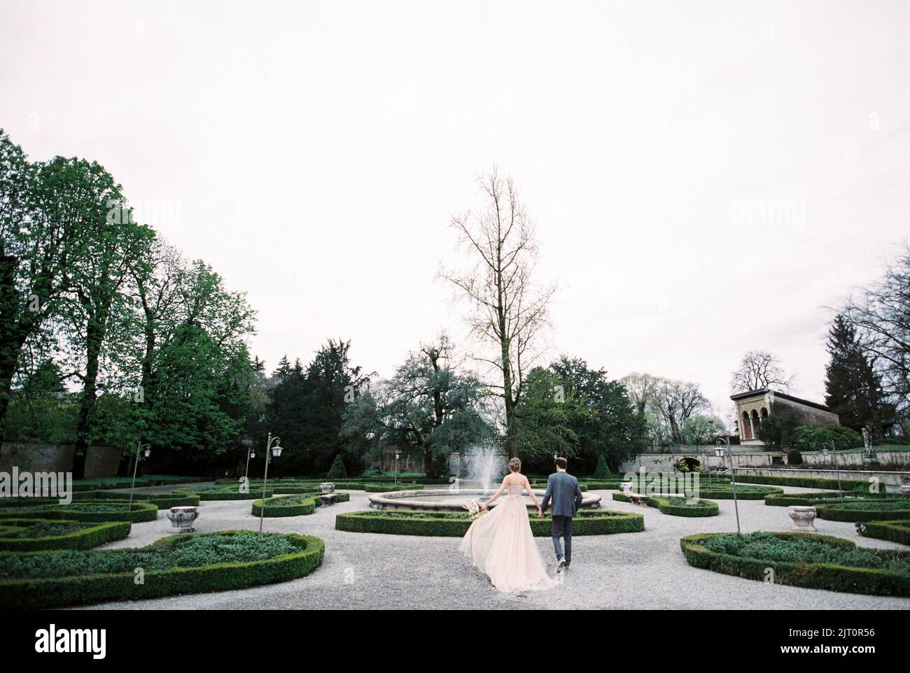 Bride and groom walk through the park holding hands. Lake Como, Italy ...
