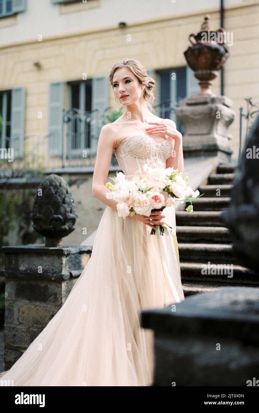Bride with a bouquet stands on the steps in front of an old villa. Como ...