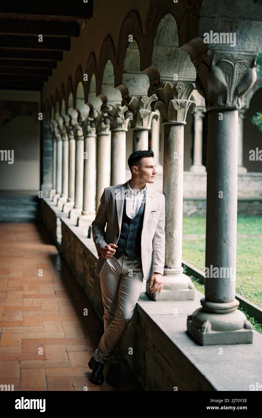 Man in a suit stands near the columns on the terrace of an old villa ...