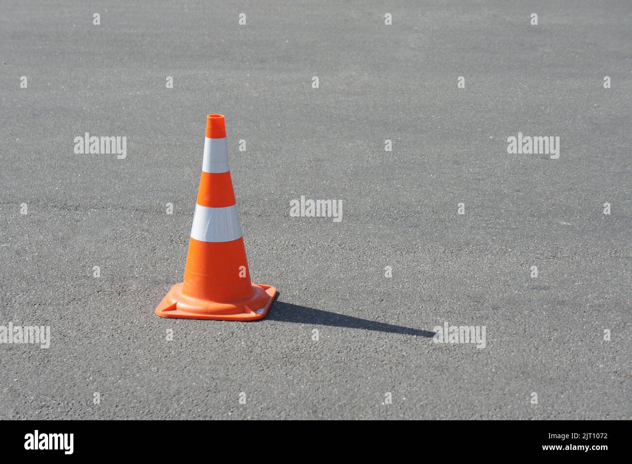 traffic cone, with white and orange stripes on gray asphalt, copy space ...