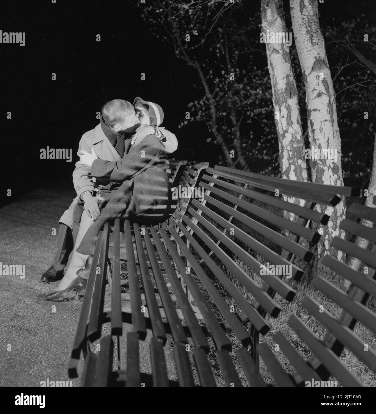 In the 1950s. A young couple is sitting on a bench kissing. A date ...