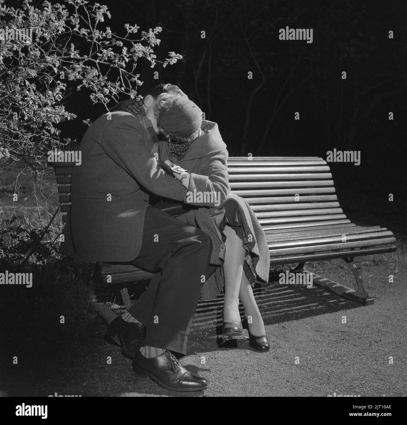 In the 1950s. A young couple is sitting on a bench kissing. A date ...