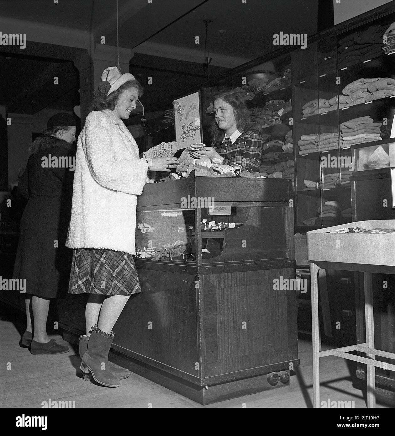 Shopping in the 1940s. A young woman in a store where a sales woman is ...