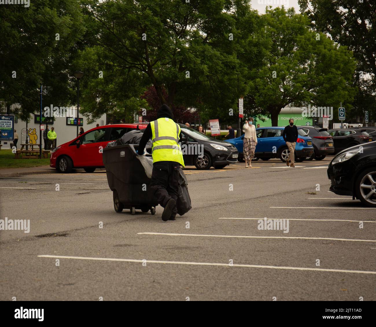The urban infrastructure worker pushing a full black wheelie bin across ...