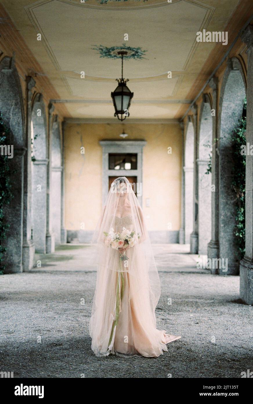 Bride in a dress with a veil stands with a bouquet on the terrace of an ...