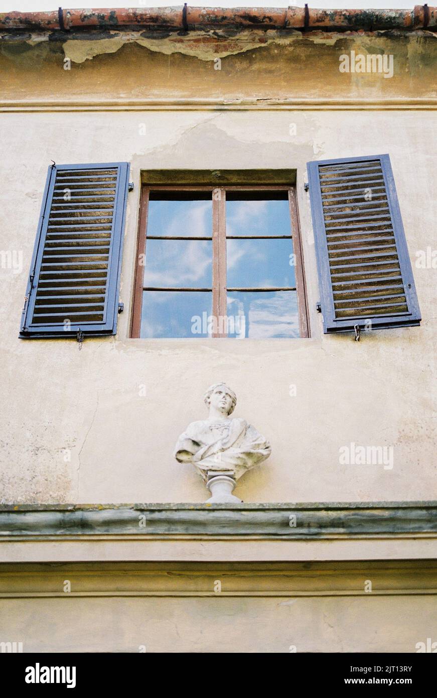 Statue on a parapet under a shuttered window on the facade of an old ...