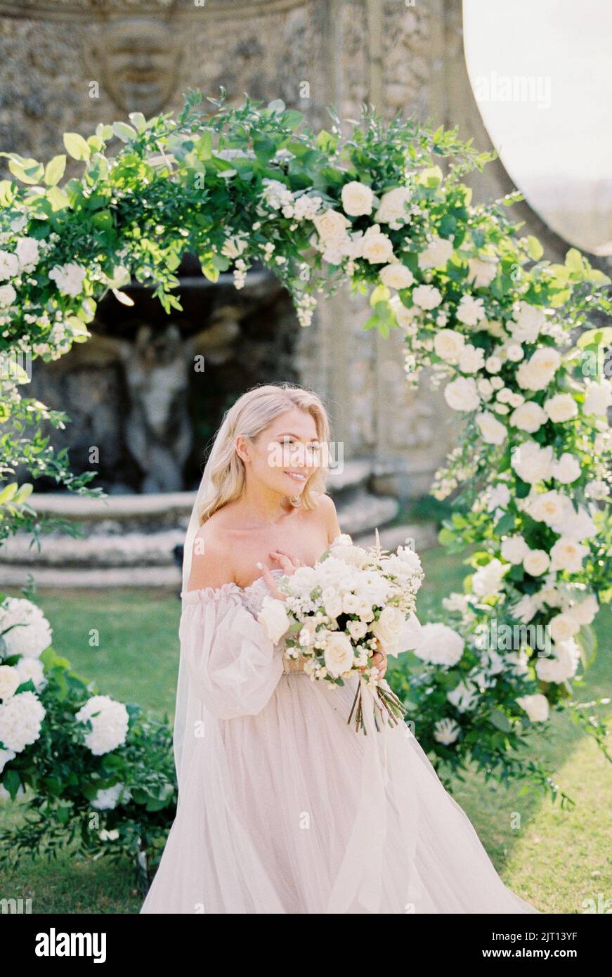 Bride in a veil with a bouquet stands at the wedding arch Stock Photo ...