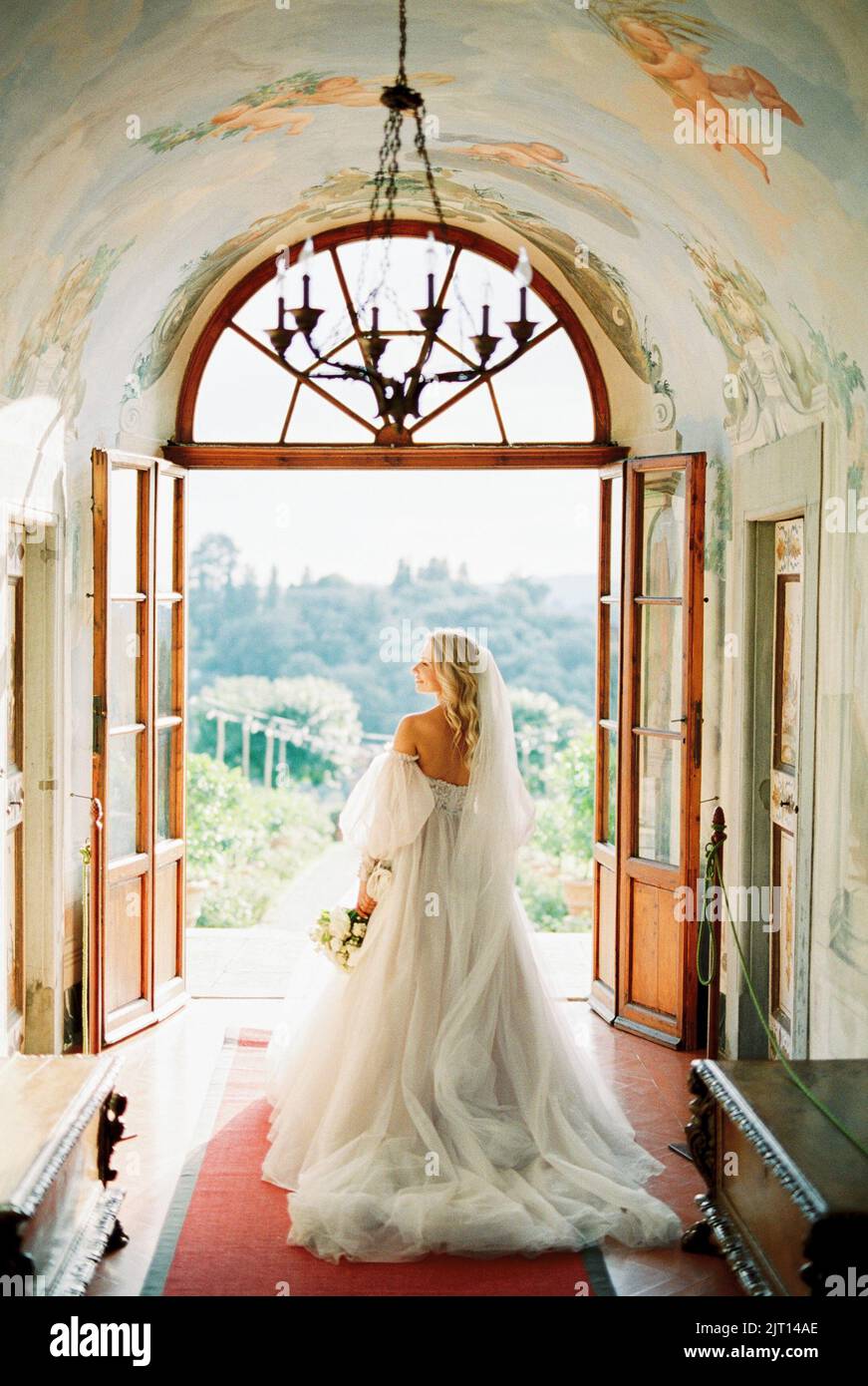 Bride in a white dress stands at the open door of an old villa ...