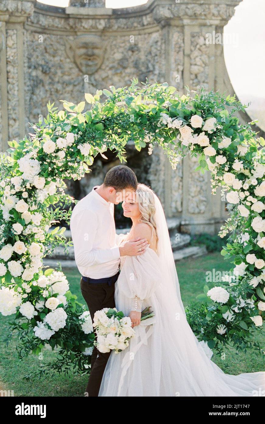 Bride and groom are standing near the wedding arch in front of the ...