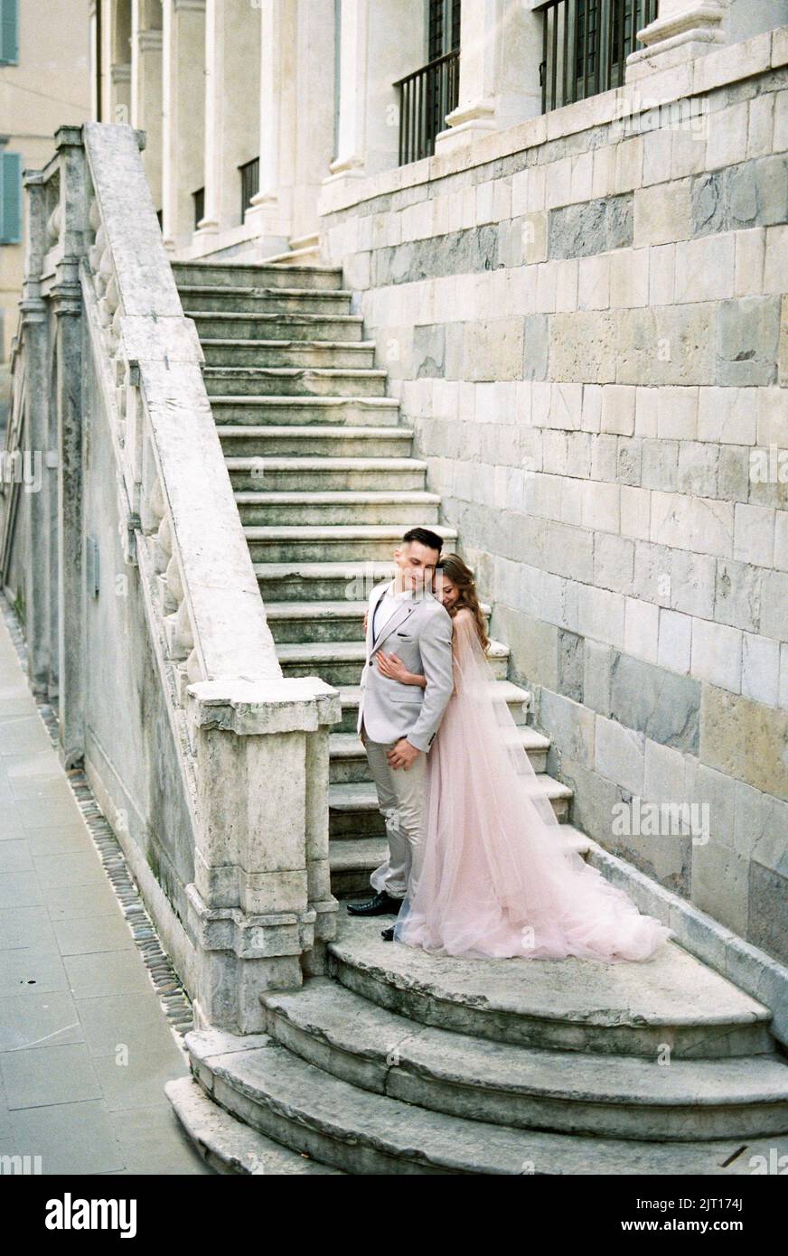 Bride hug groom from behind on the stone steps of a building. Bergamo ...