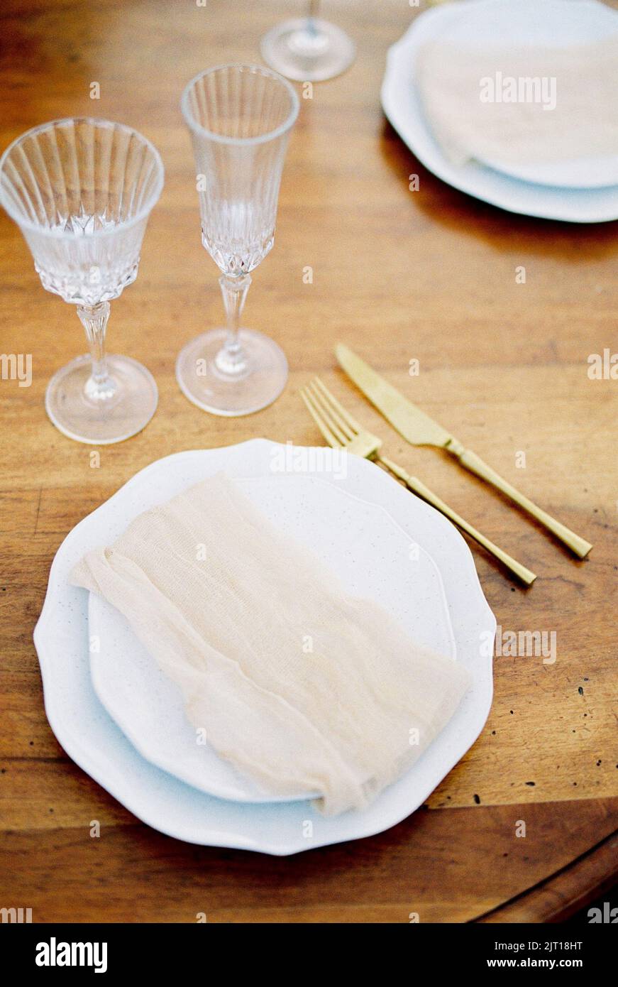 Ribbon on a plate next to cutlery and wine glasses on a wooden table ...