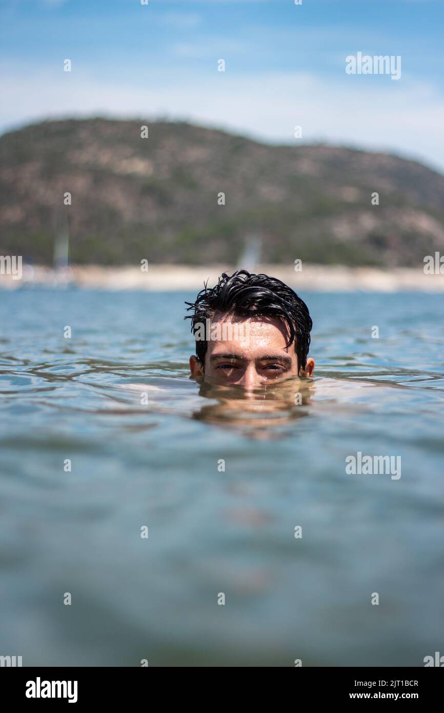 Handsome Caucasian man submerged in water. He is on a beach and you can ...