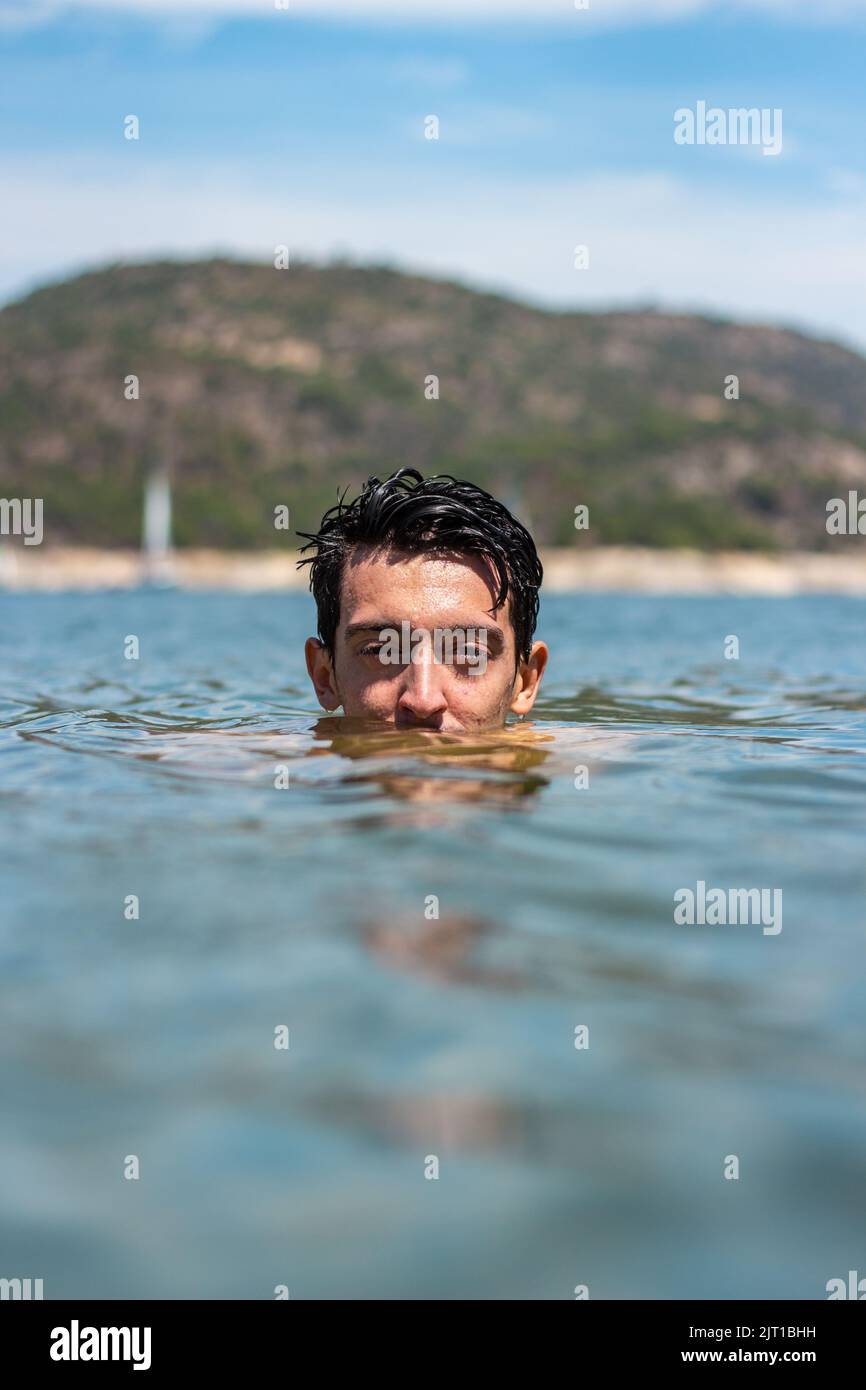Handsome Caucasian man submerged in water. He is on a beach and you can ...