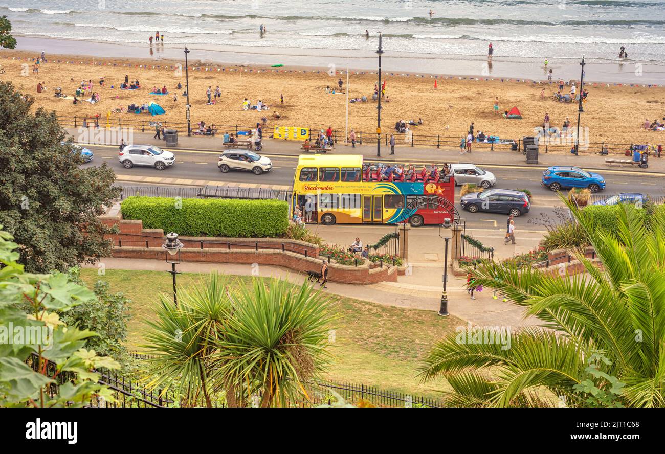Downward view of a seaside promenade and beach. There are gardens in ...
