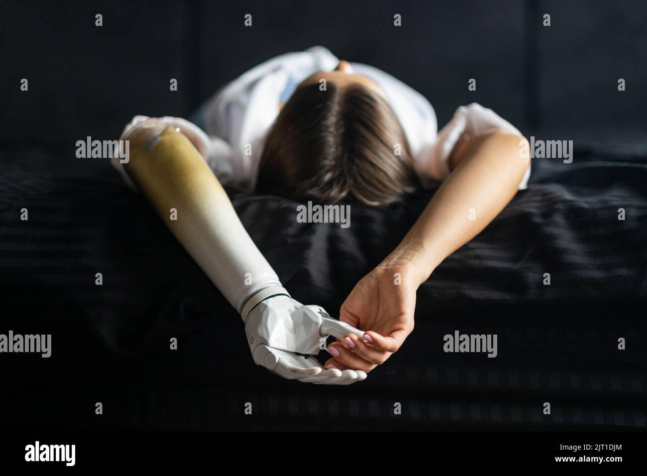 Close up two hands of woman with bionic arm on black bed at home ...