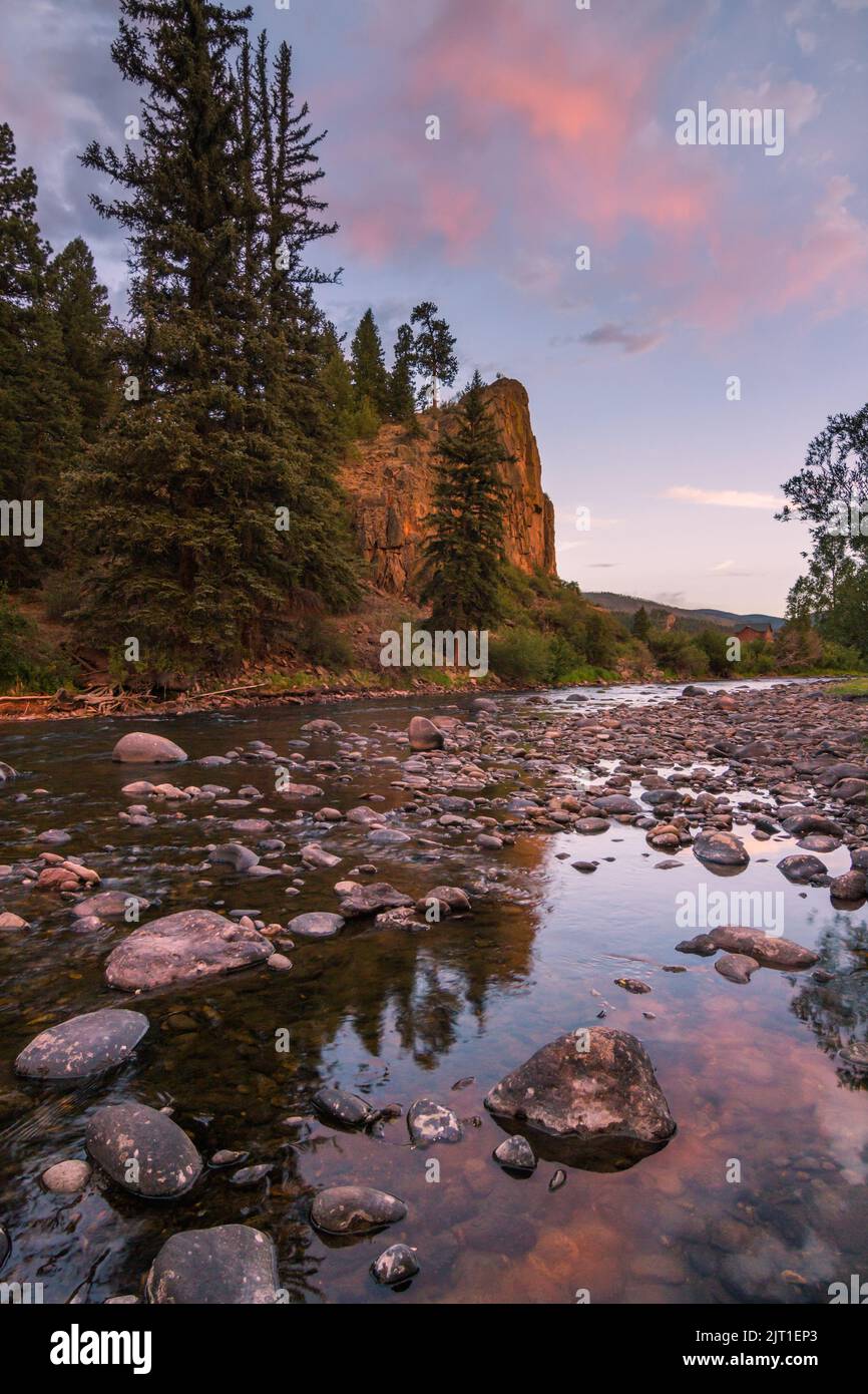 A sunset of pink clouds is reflected off the smooth water and stones of ...