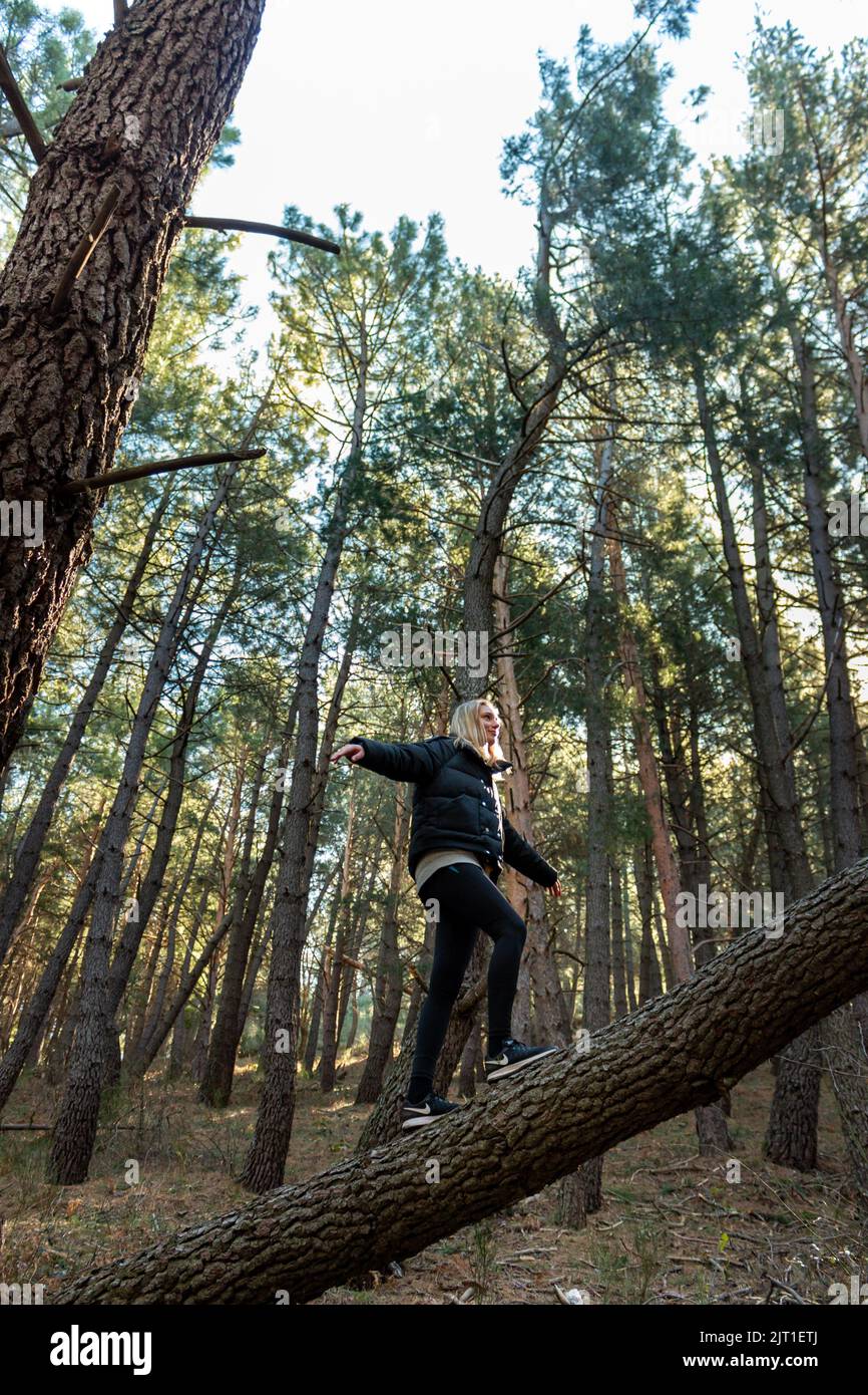 blonde woman walking on top of a pine trunk in the middle of nature ...