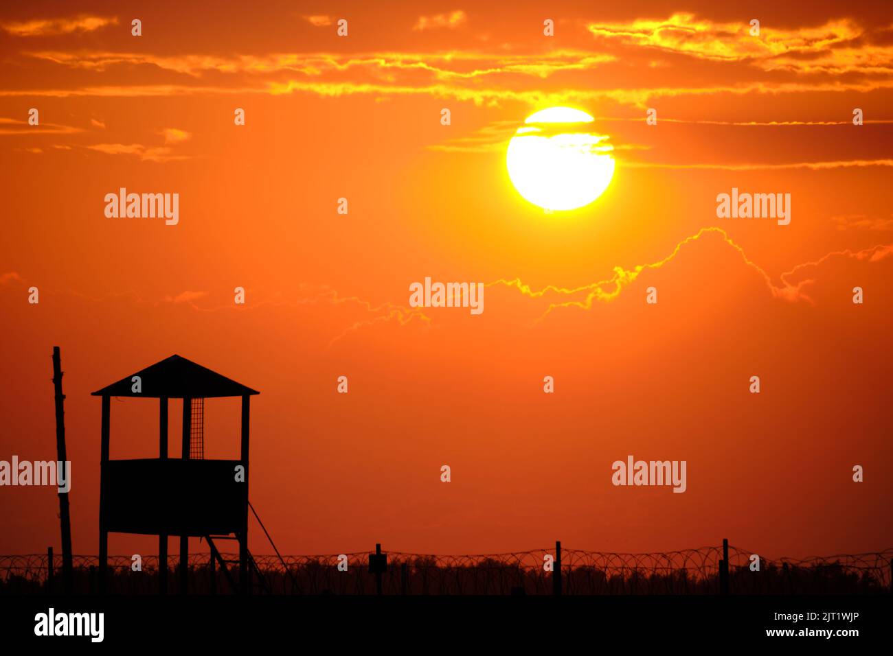 Fence with barbed wire and an old watchtower background bright sun and ...