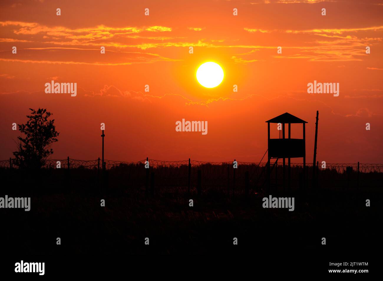 Fence with barbed wire and an old watchtower background bright sun and ...