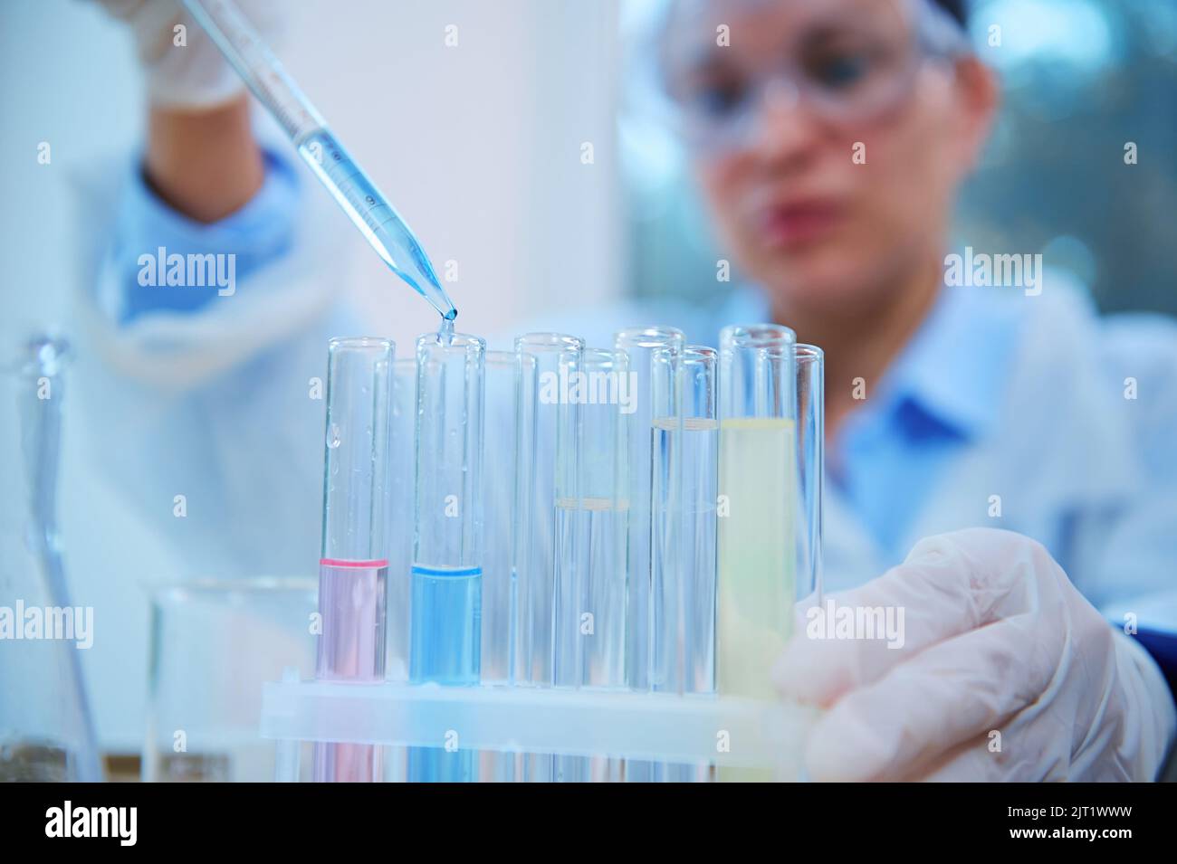 A drop of blue liquid dripping from pipette into test tube over blurred ...